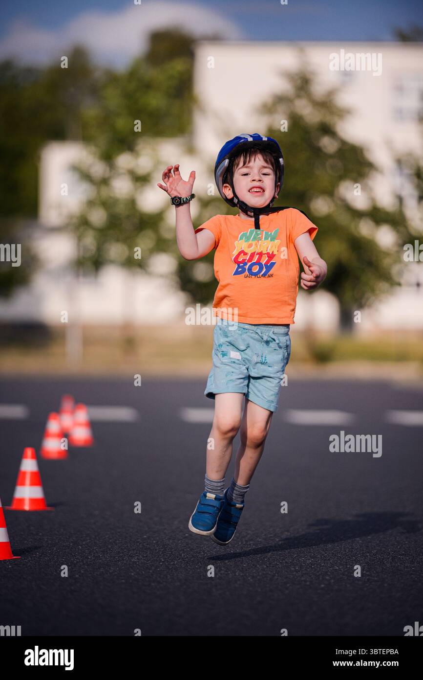 Energetic child in a helmet jumps mid-air on a city street near cones ...