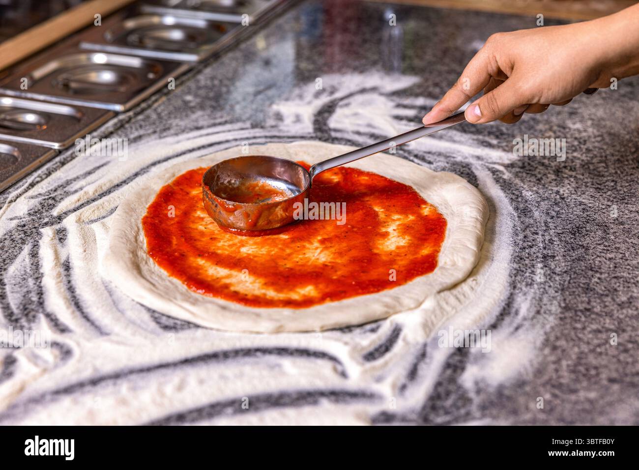 Process of preparing pizza. Chef pours tomato sauce over the rolled ...