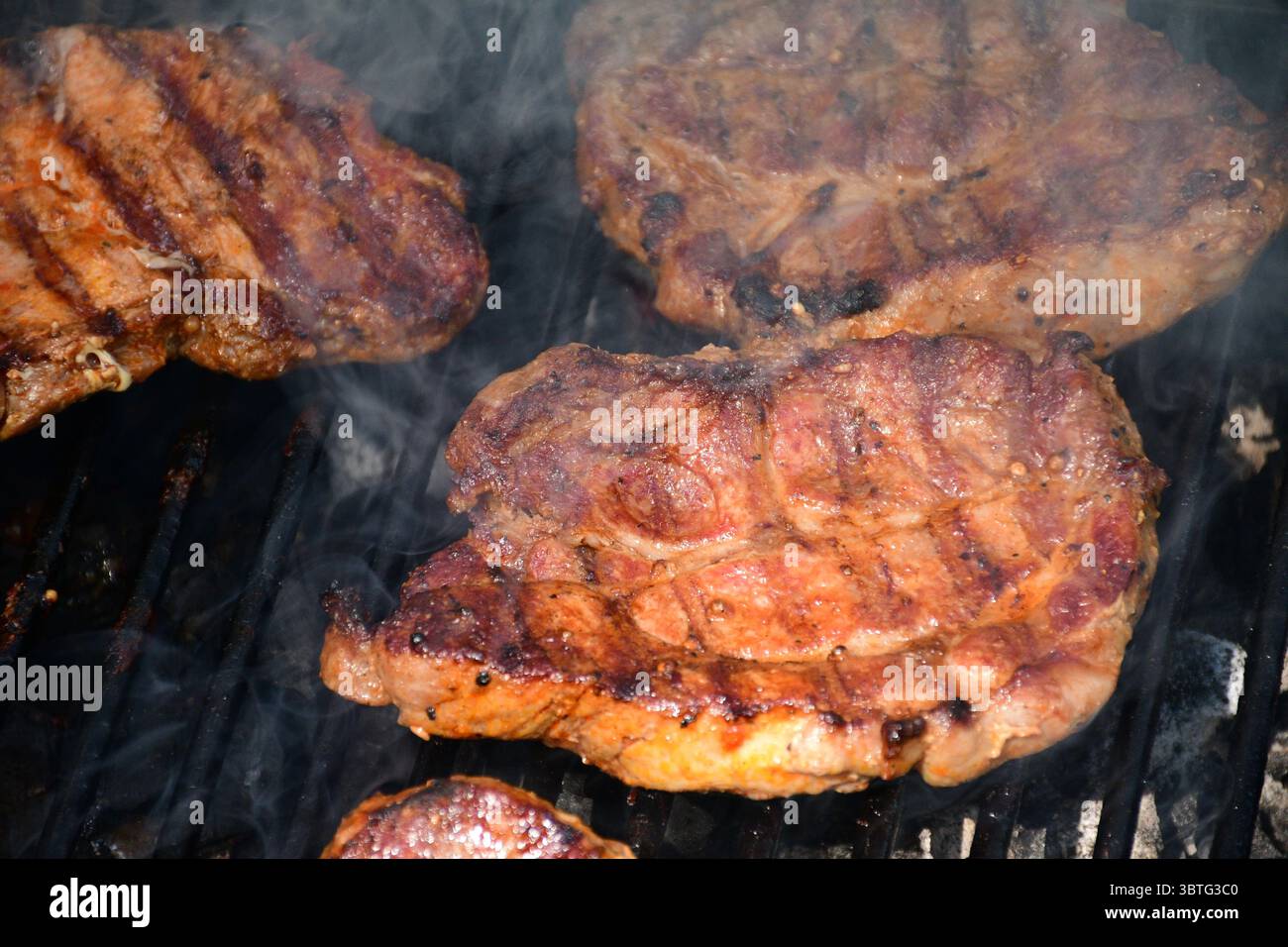 Grilled pork steaks on barbecue with smoke and char lines in a close-up ...