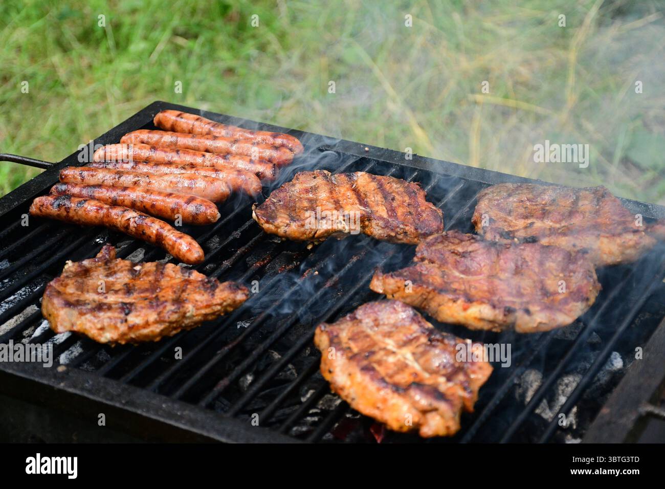 Smoky grill loaded with sausages and pork steaks sizzling over hot ...