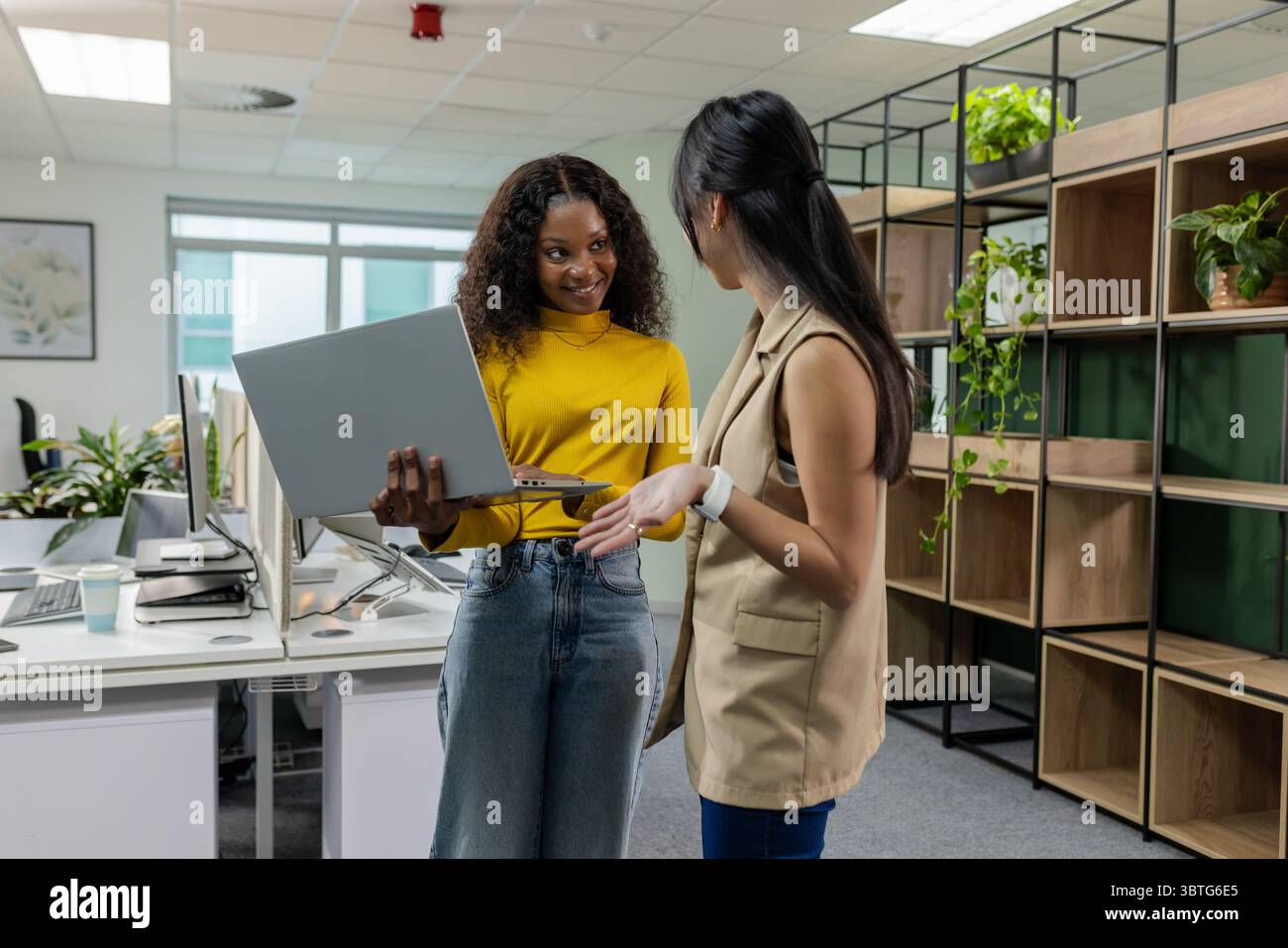Diverse female coworkers standing in modern open-plan office holding ...