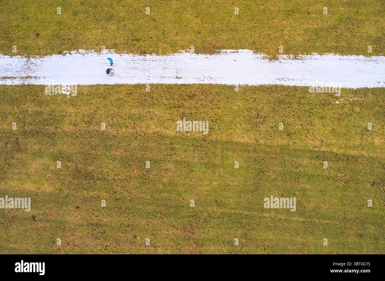 Aerial view of a solitary figure braving the snowy path cutting through fields, a stark contrast ...