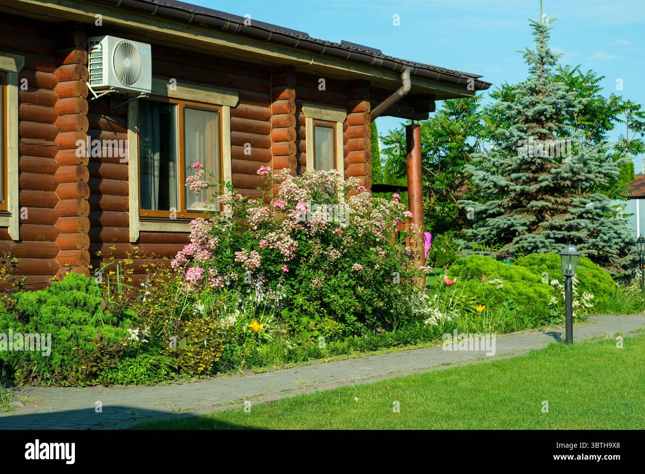 A log cabin with an air conditioner unit on the side and flowers ...