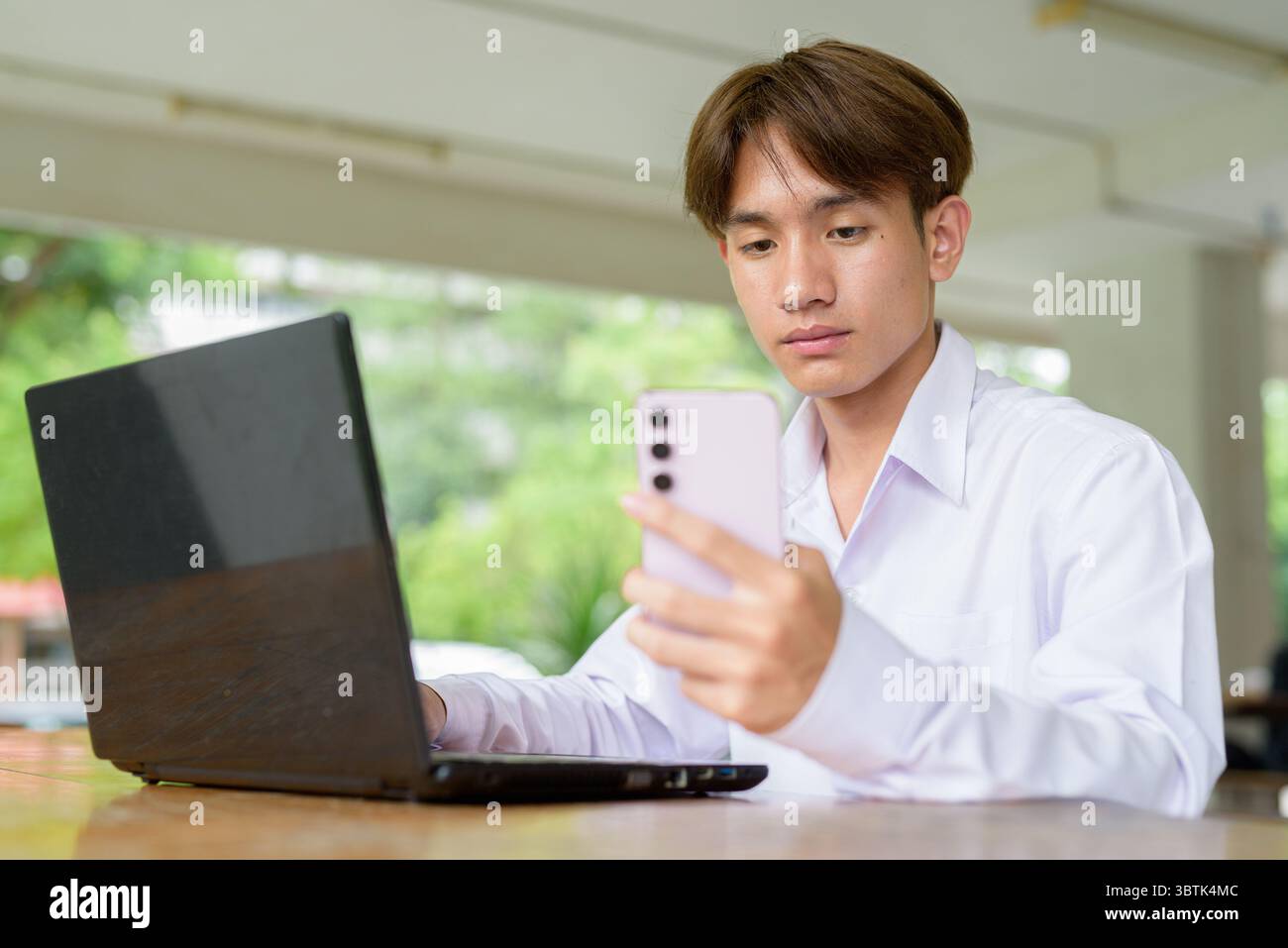 Non binary Asian university student in college campus using computer ...