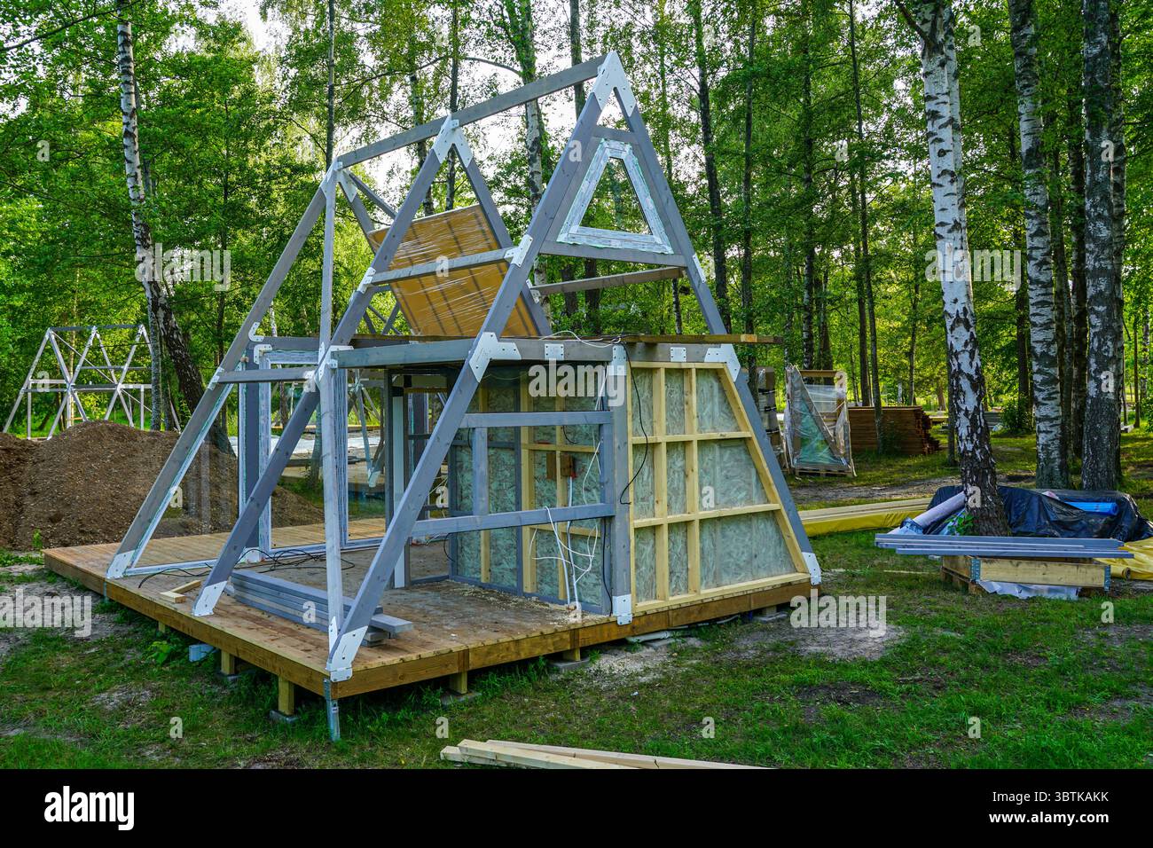 A new A-frame glamping cabin is under construction in a serene forest ...