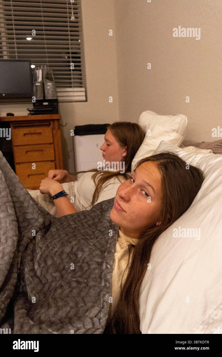 Two girls are comfortably laying on a cozy bed beneath a warm blanket ...