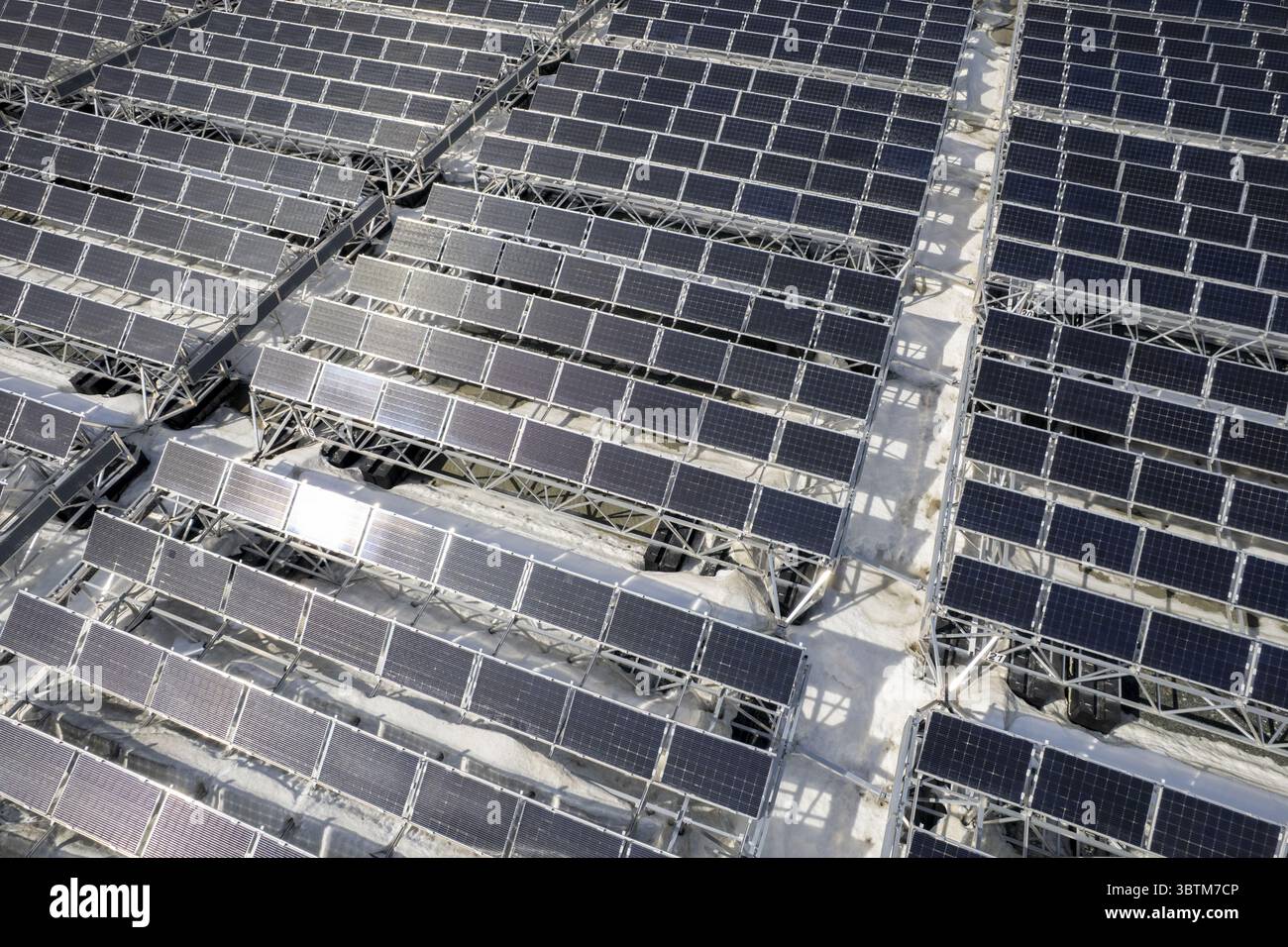Aerial view of a sprawling solar panel farm, reflecting the sun's glare ...