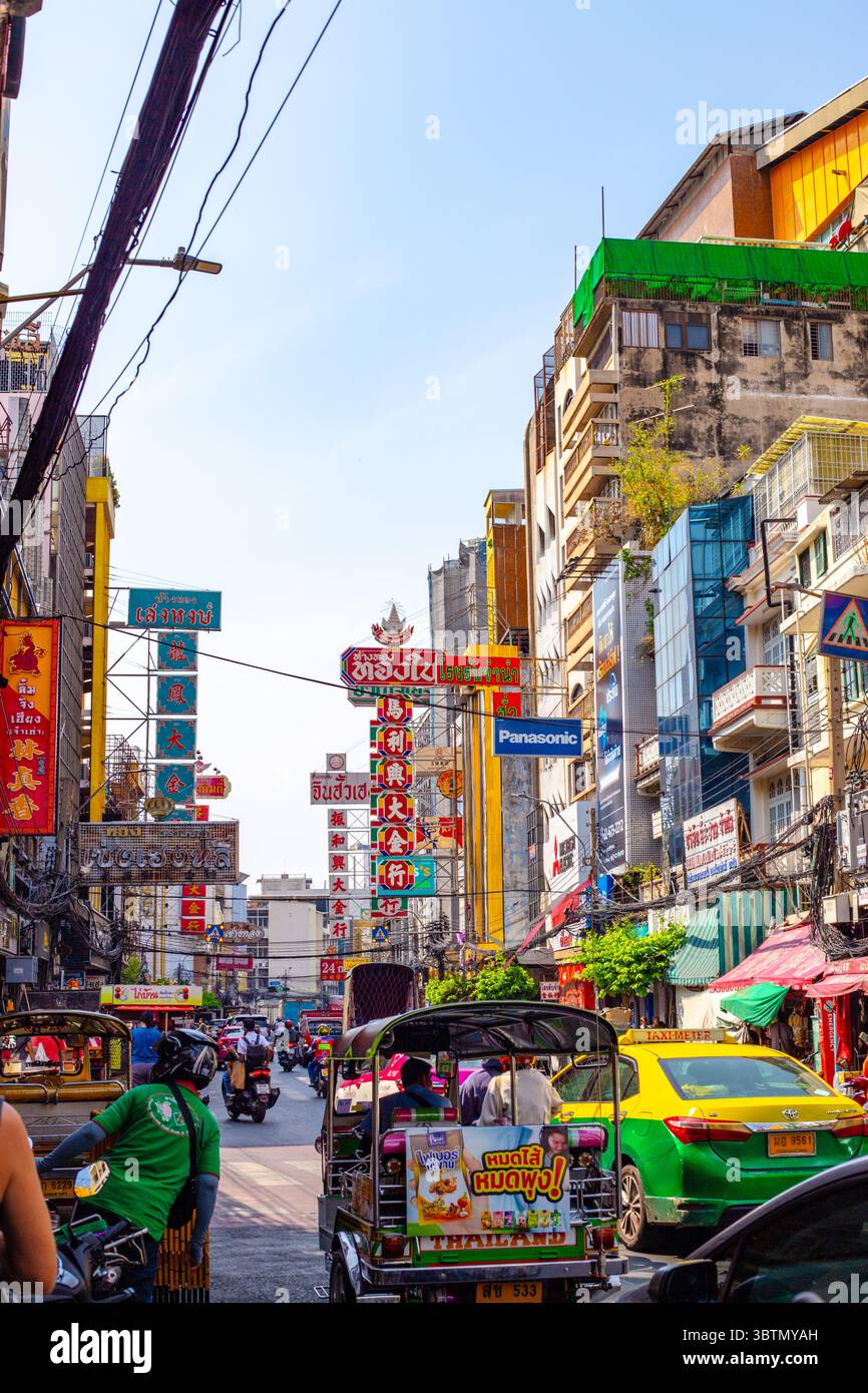 A busy street in Bangkok's Chinatown is full of colorful signs, tuk ...