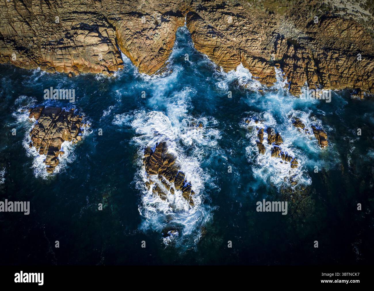 Aerial view of where turquoise waves crash against rugged, rust-colored ...