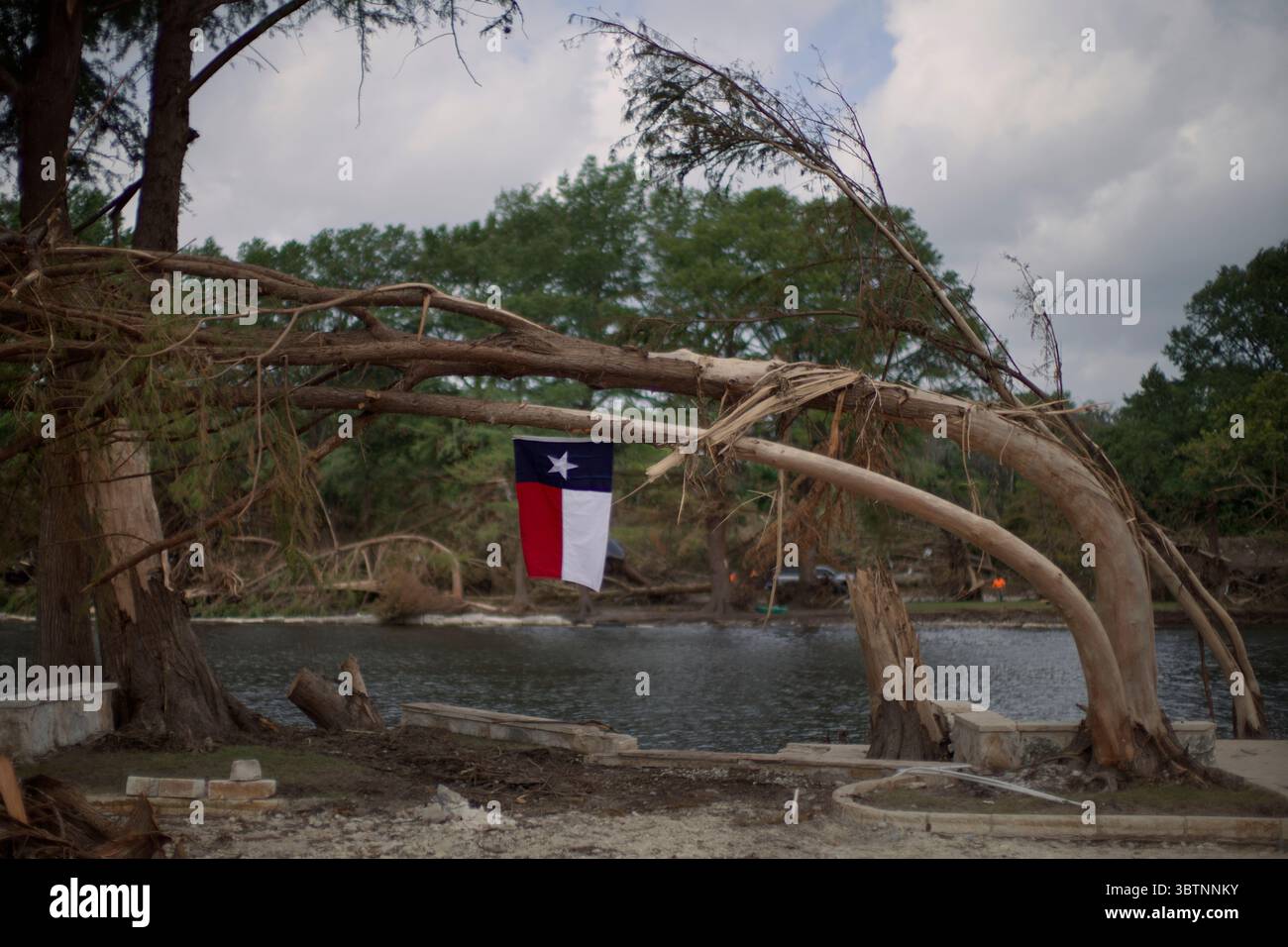 A Texas flag hangs from a flood-damaged tree on the bank of the ...