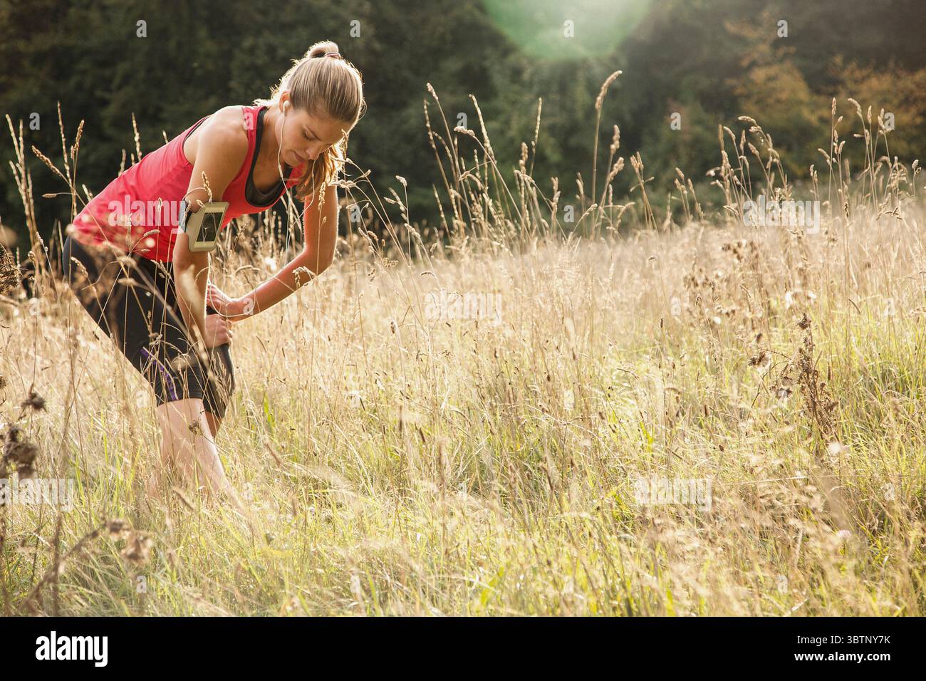 Female runner stretching leg in tall grass of summer meadow Stock Photo ...