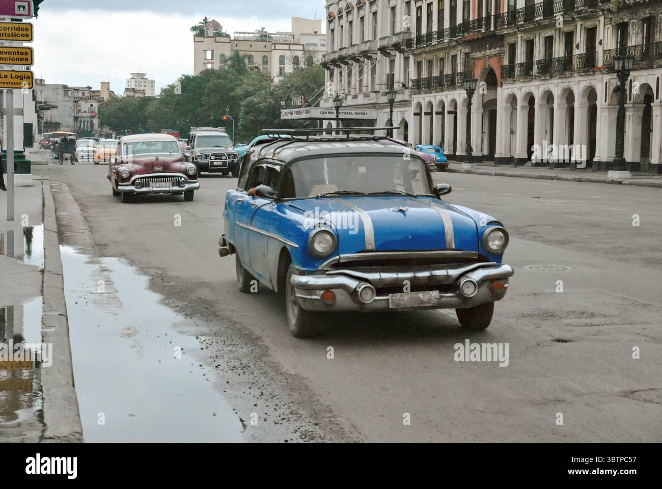 Vintage American cars driving through a historic street in Havana, Cuba ...