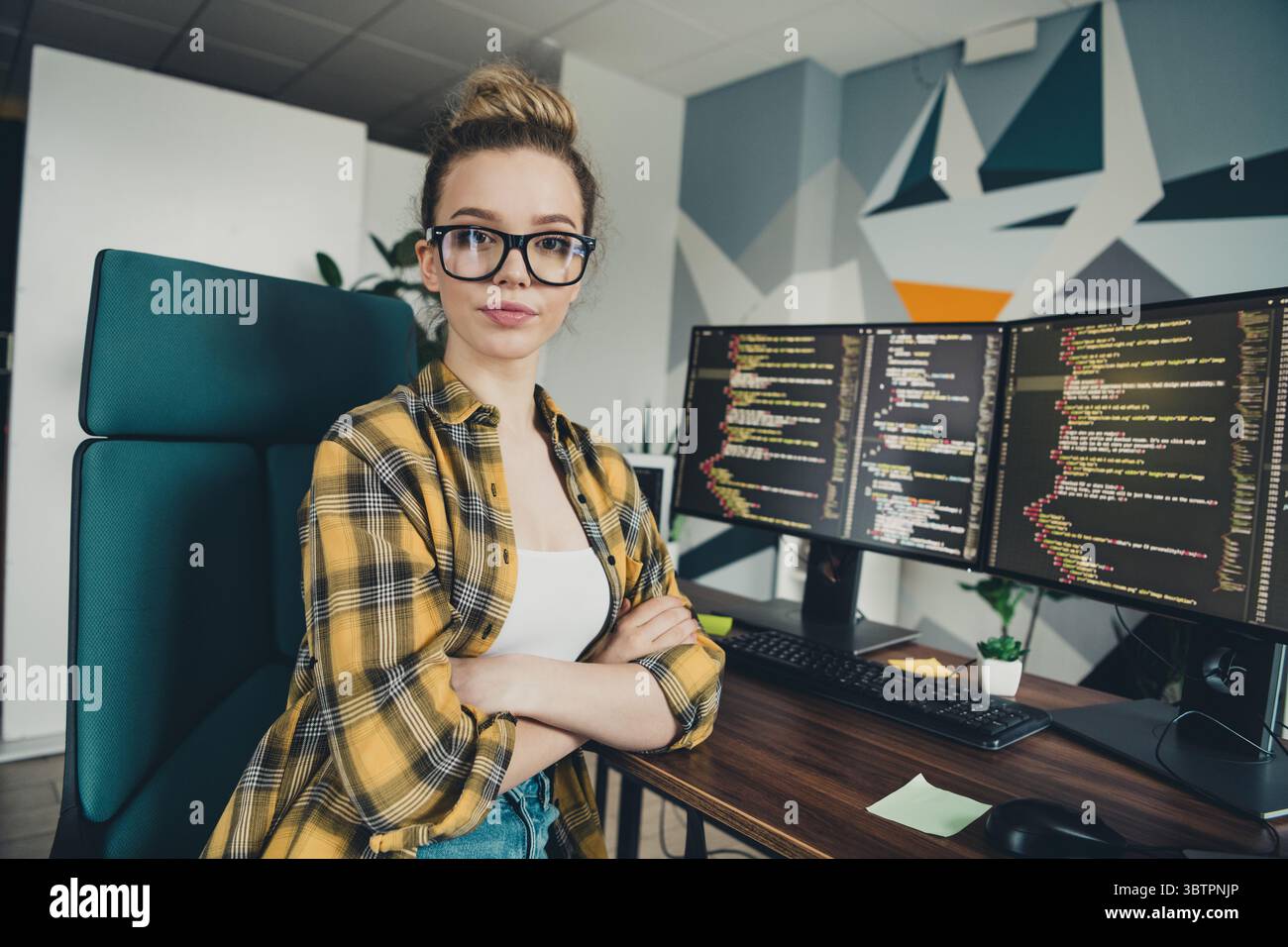Young female programmer working in a casual environment with a dual-monitor desktop setup ...