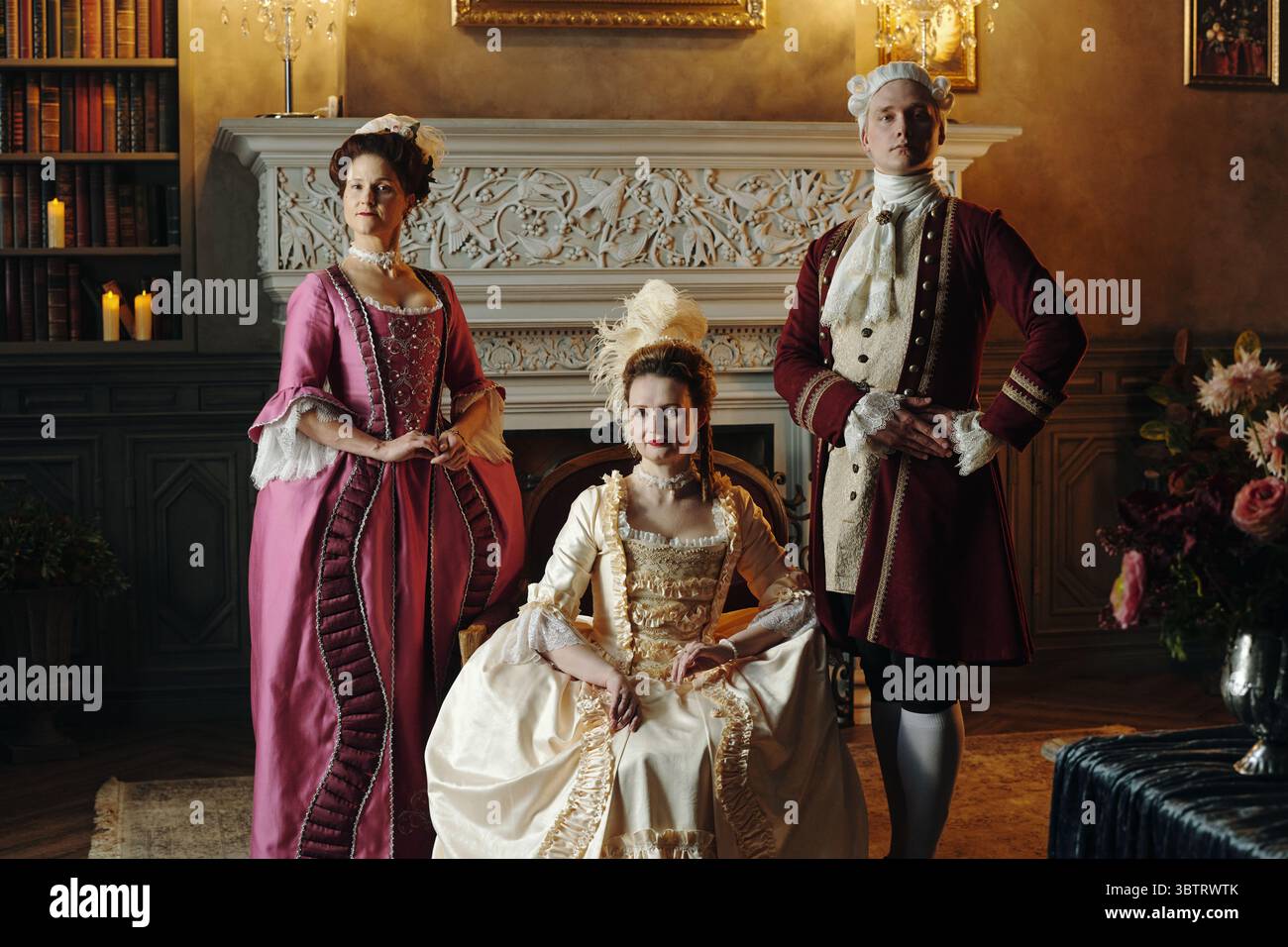 Three Caucasian adults in Baroque period costumes posing in ornate ...