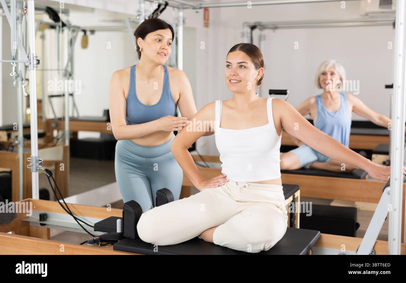 Asian female pilates trainer controlling movements of young woman on ...