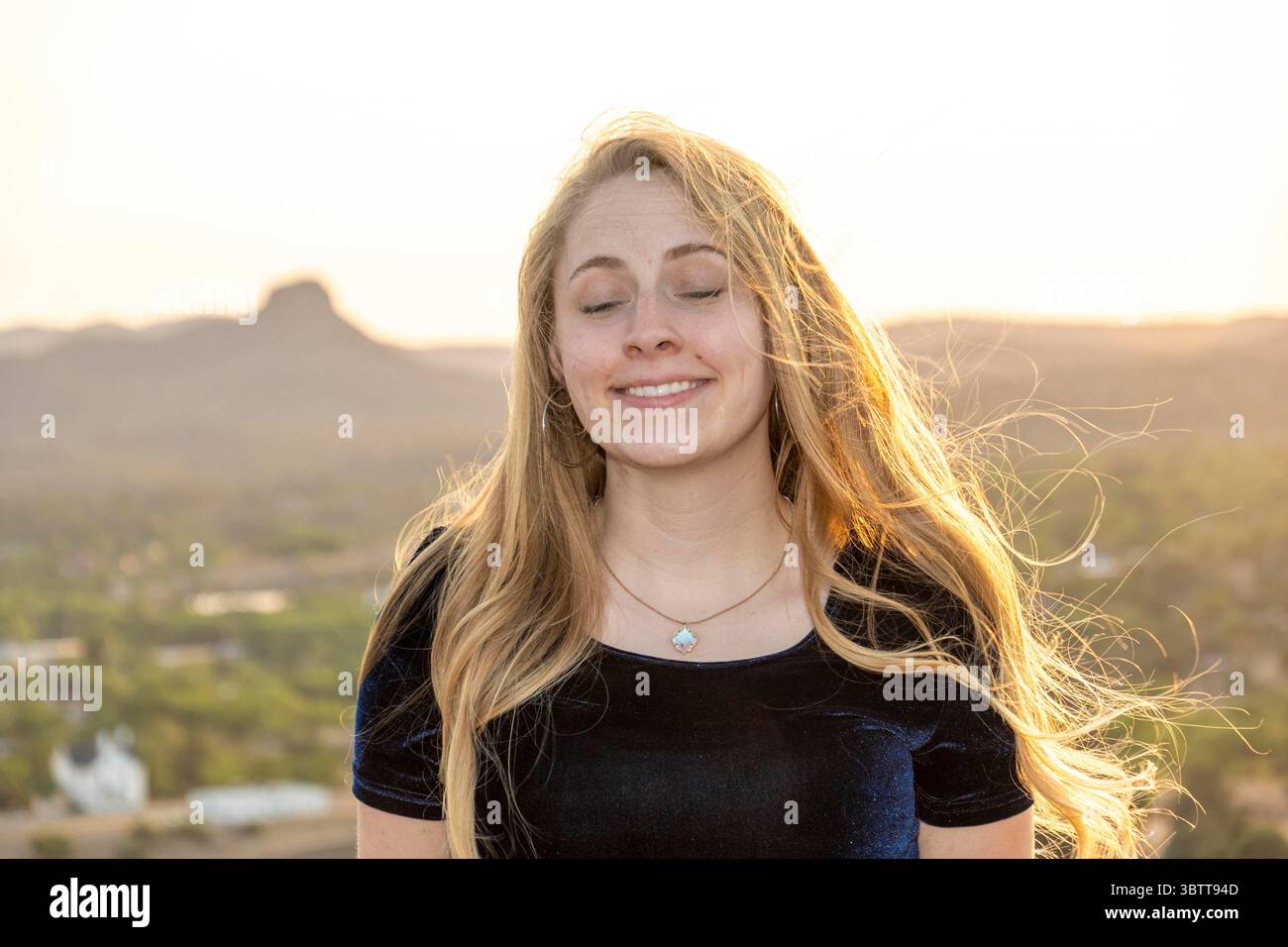 A young woman stands with her eyes gently closed, allowing the wind to ...