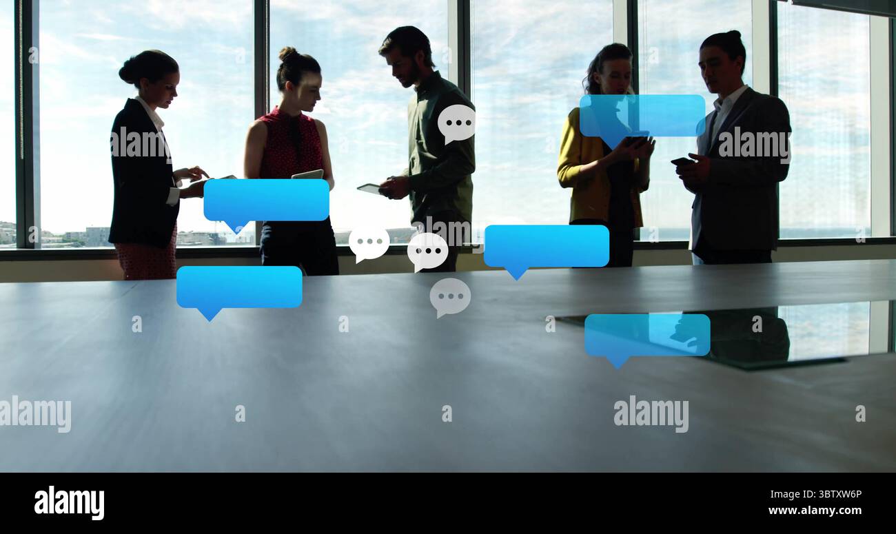 Standing business team chatting on smartphones and tablets in ...