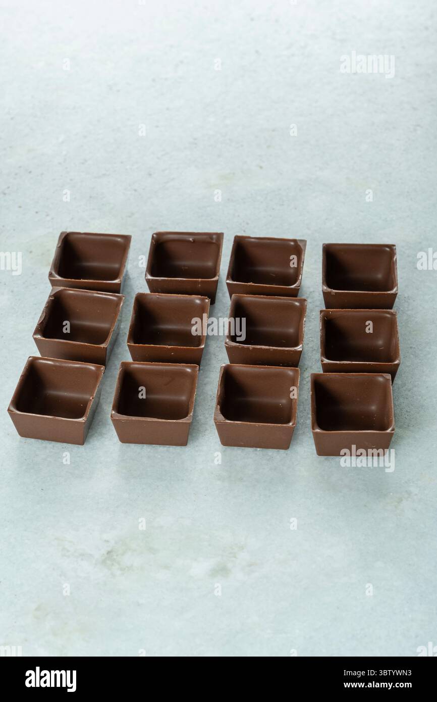 Square-shaped milk chocolate shells ready to be filled vertical Stock ...