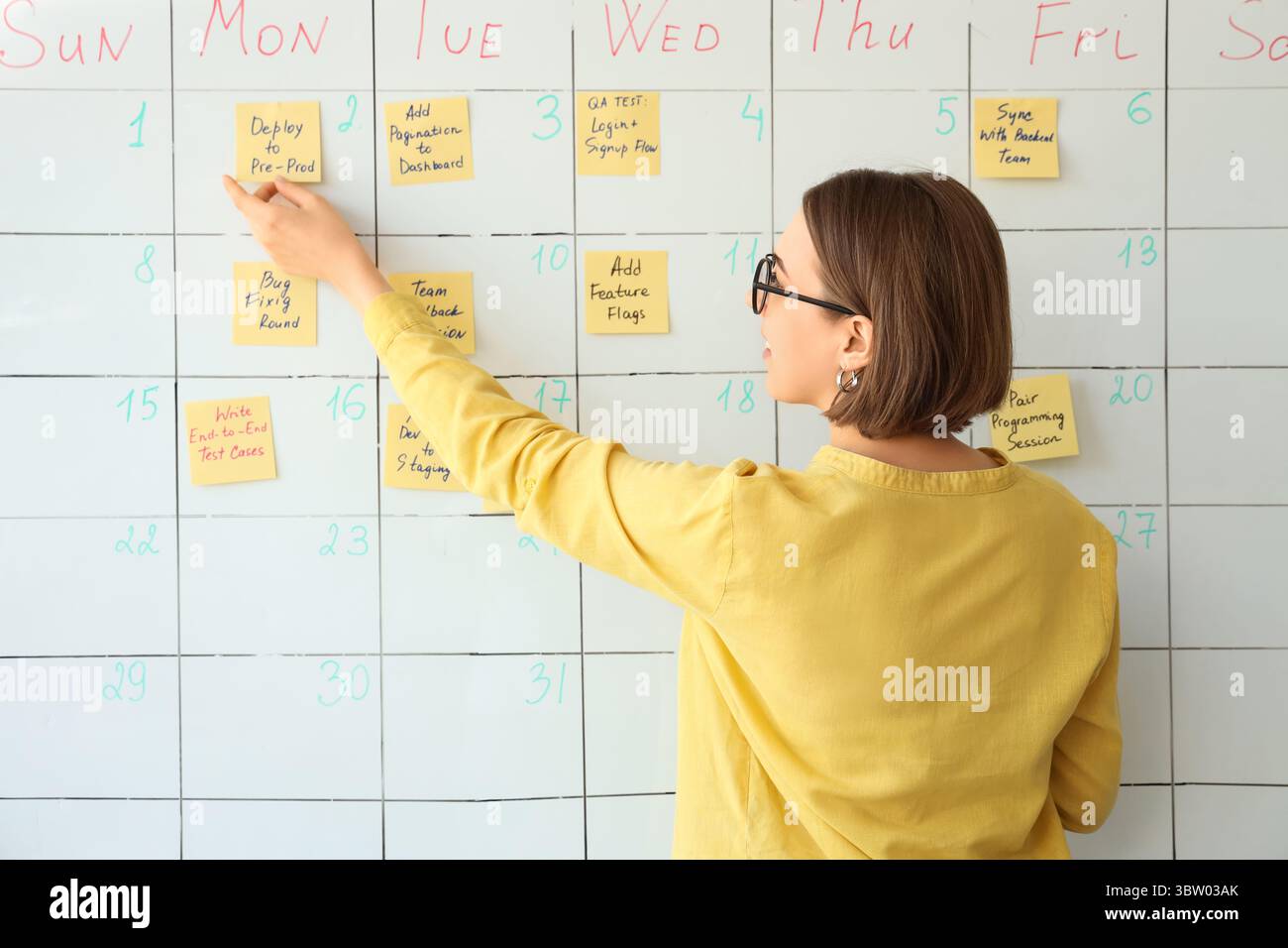 Young woman sticking note with plans on whiteboard in office, back view ...