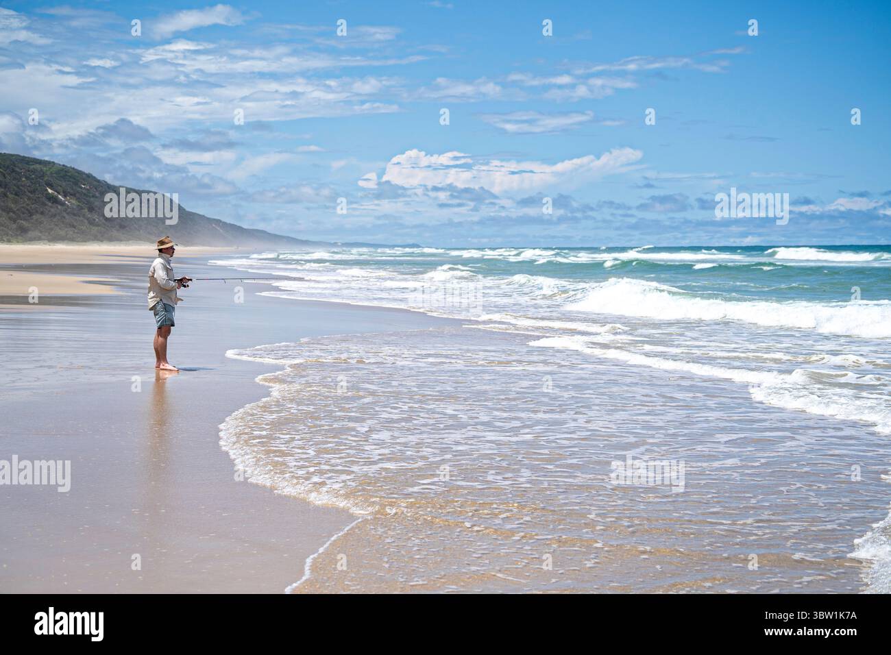 Lone fisherman fishing on wide sandy beach. Teewah Beach, Great Sandy ...