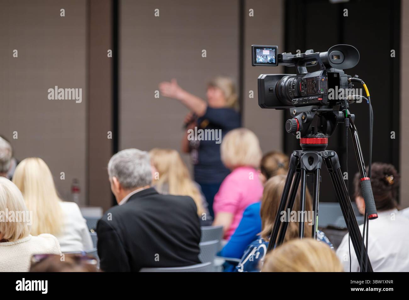 Camera filming a speaker addressing an audience during a formal ...