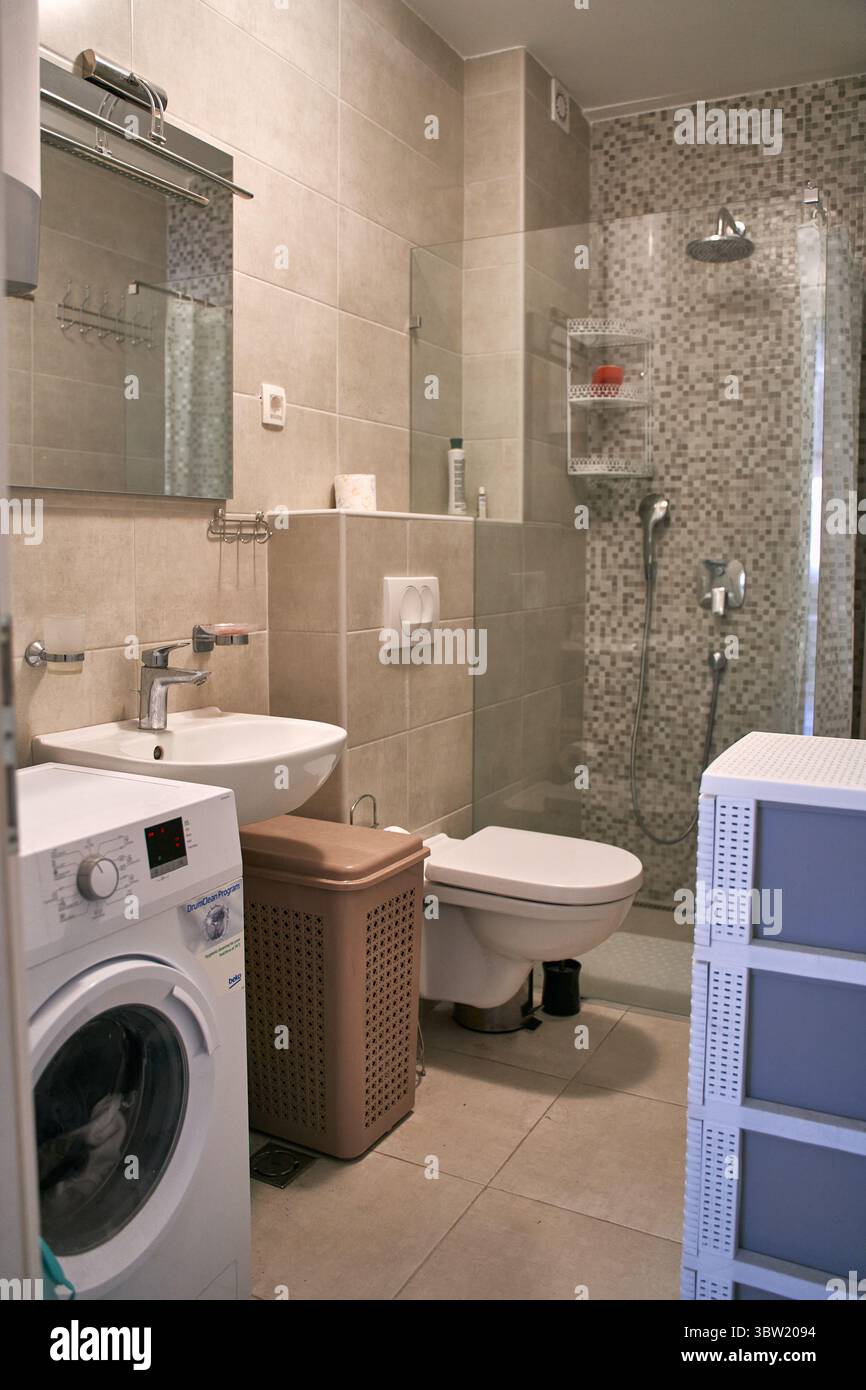 A compact modern bathroom featuring a shower, washing machine, sink ...