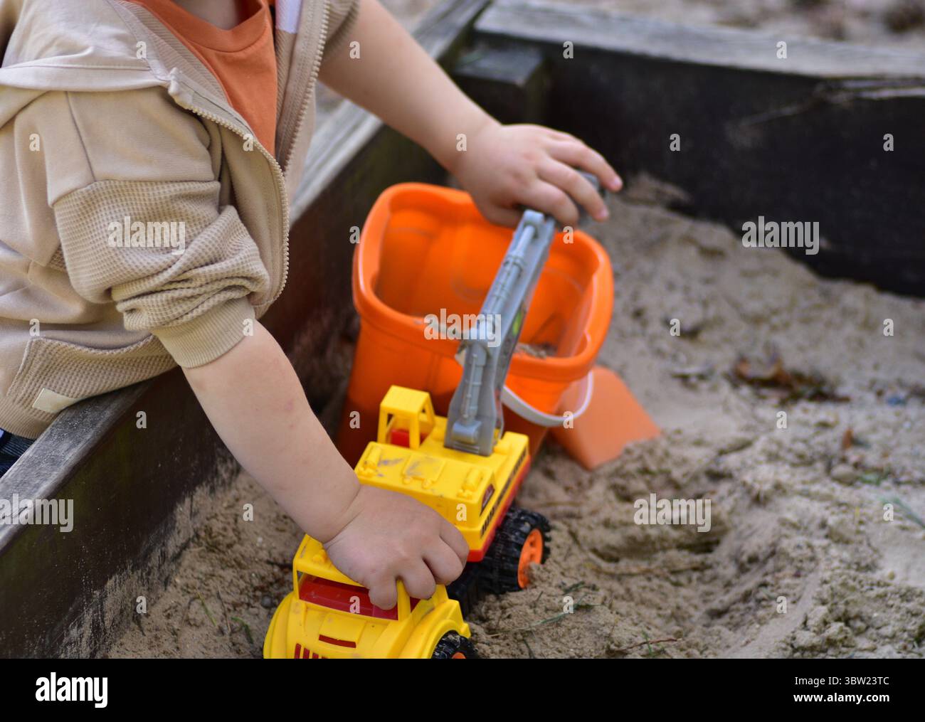 Child playing in a sandbox with a yellow toy excavator and orange ...