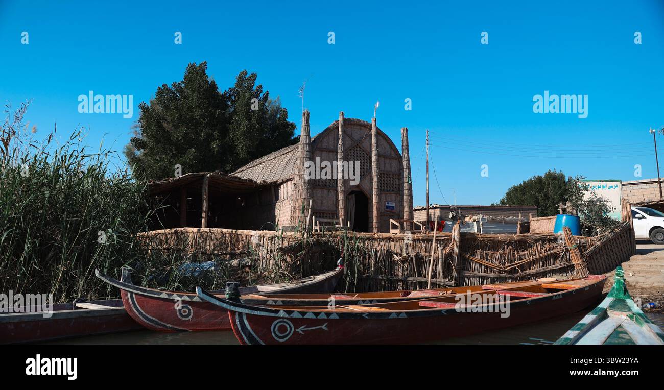 Traditional reed houses stand alongside colorful boats in the ...