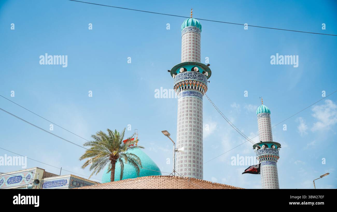 Two tall minarets rise above the landscape in Kufa, Iraq, with palm ...