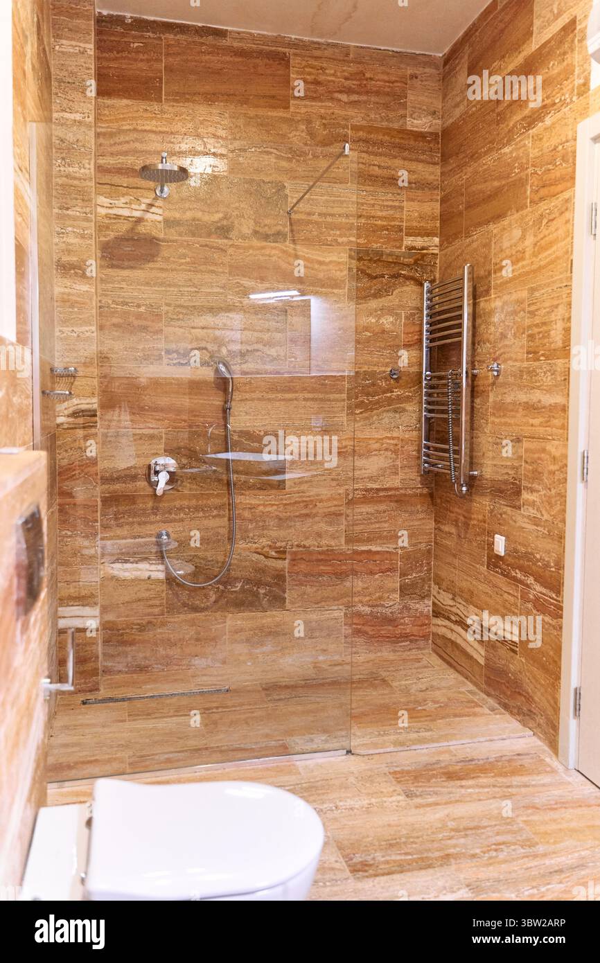 A modern walk-in shower features a glass enclosure and brown tile ...