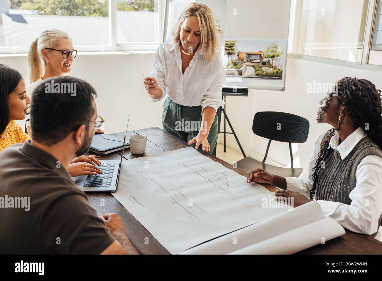 Architectural team discussing building plans in a bright office, including four women and one ...