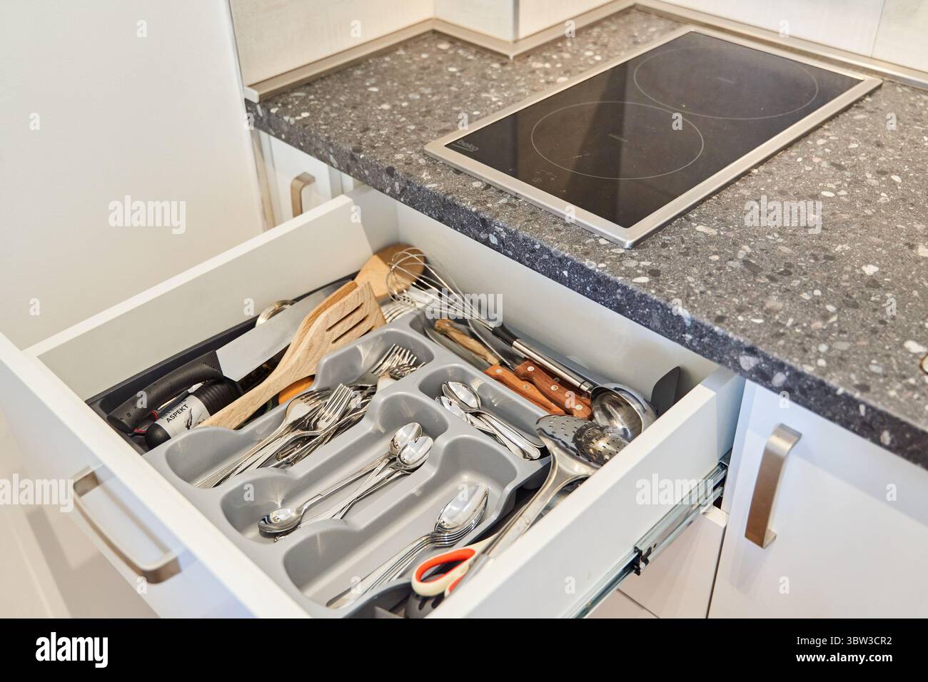 Open kitchen drawer with cutlery and utensils near a granite countertop ...