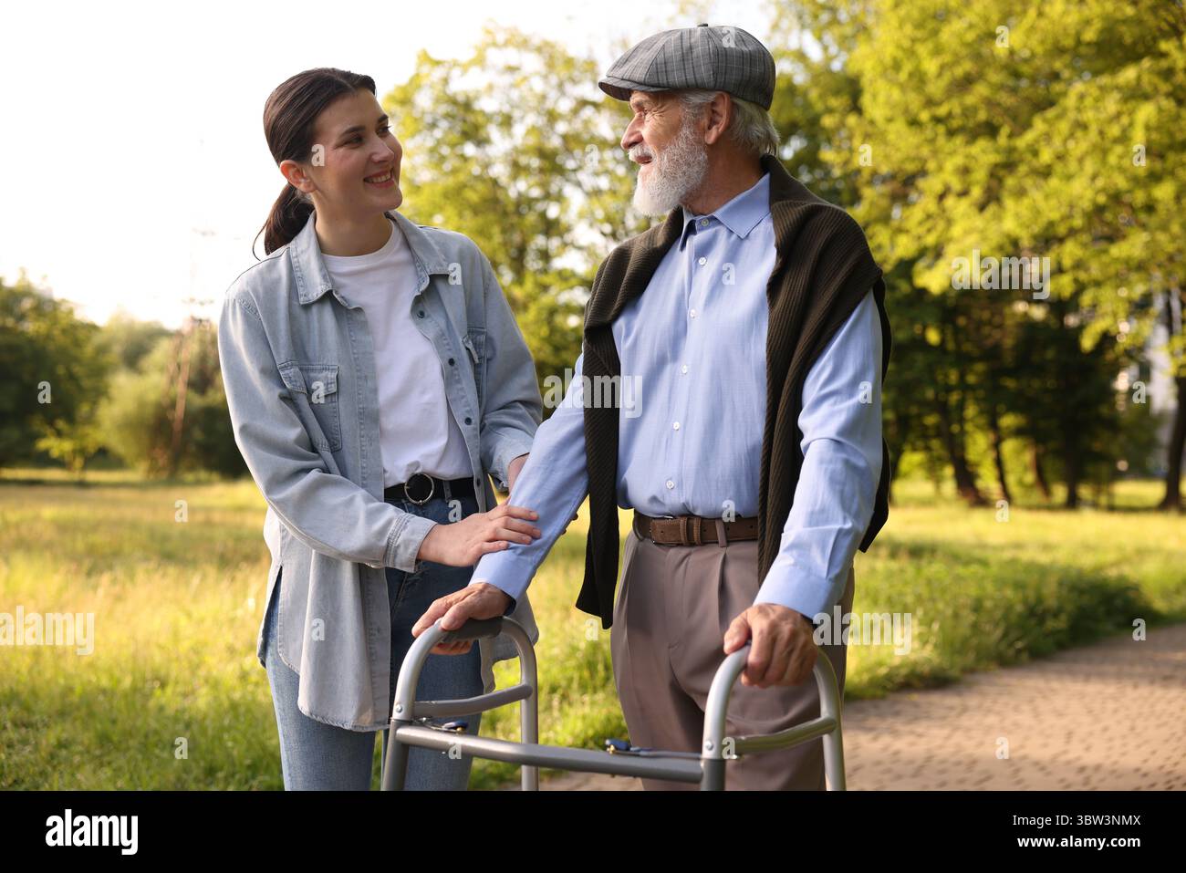Smiling caregiver supporting elderly man who using walking frame ...