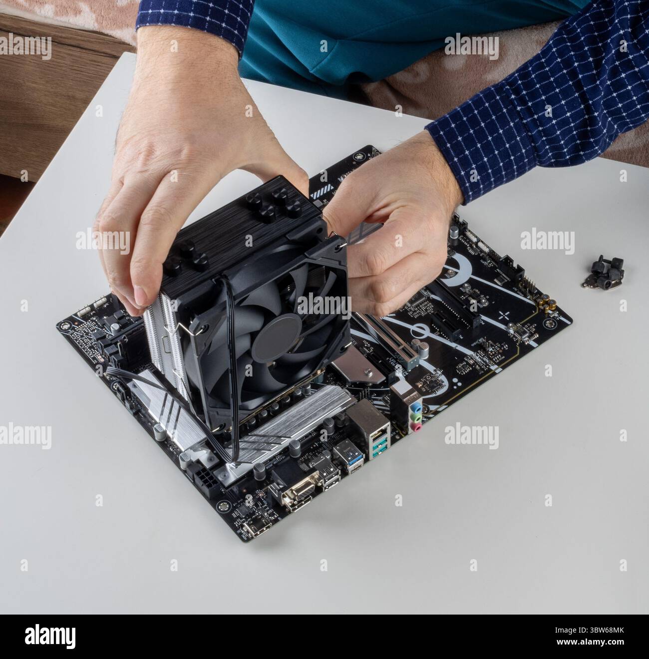 the hands of a man installing a fan on the CPU cooler tower on the ...