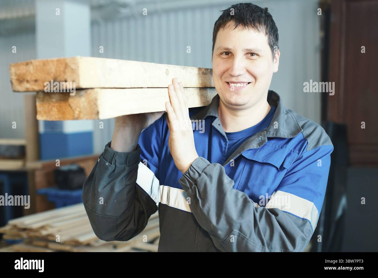 A young man stands in a carpentry shop and holds wooden bars on his ...