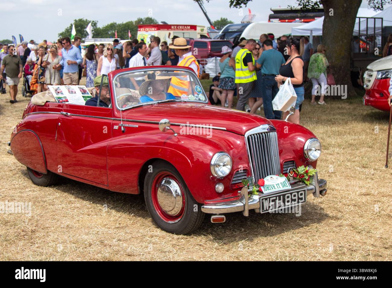 Restored red Sunbeam-Talbot 90 convertible at a UK country fair, driven past crowds during a ...