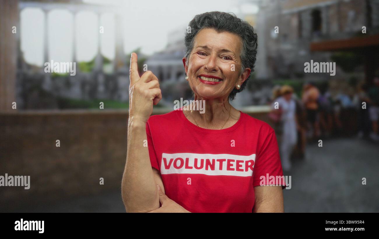 Woman with grey hair wearing volunteer shirt smiling in an urban street ...