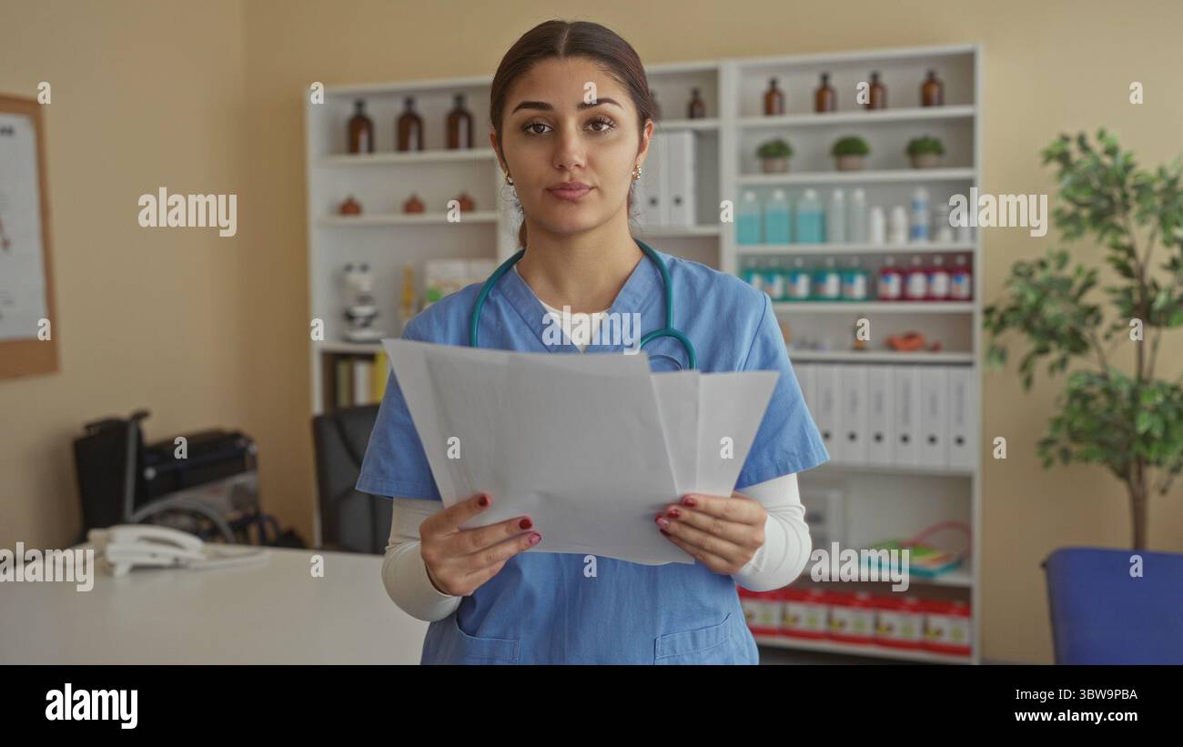 Young woman in scrubs reads documents in a hospital room indicating her ...