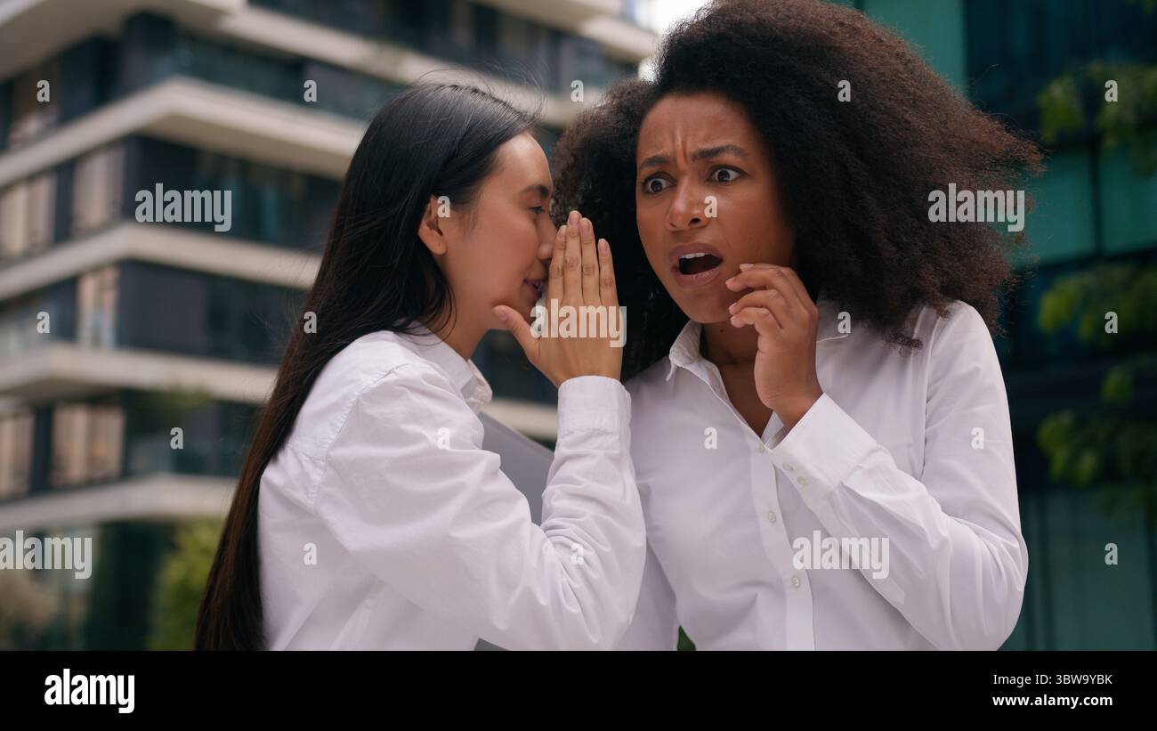 Two women African American Asian Korean girls whisper on ear secret ...