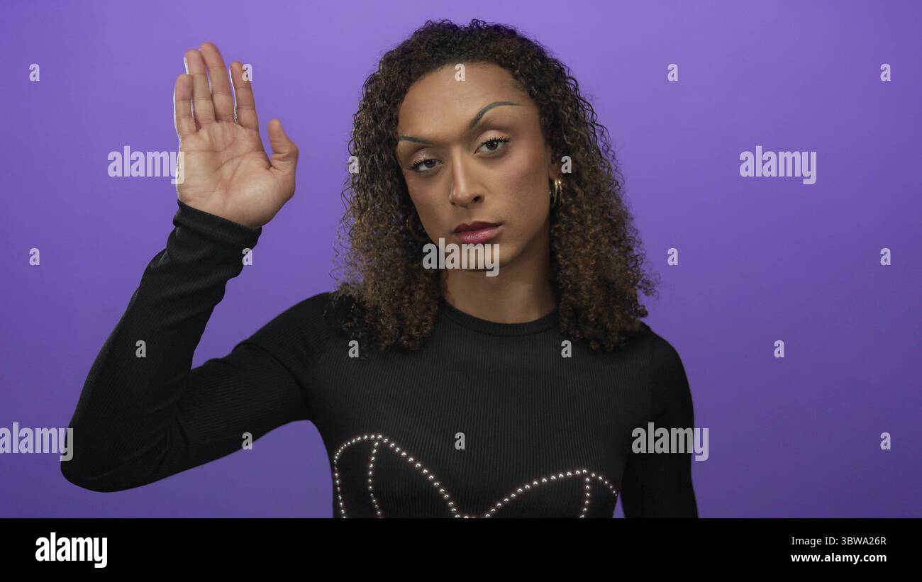 Transgender woman raises hand in purple studio space facing camera with ...