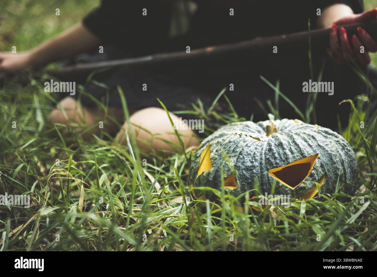 Close up of green pumpkin lantern on grass with female wizard holding ...