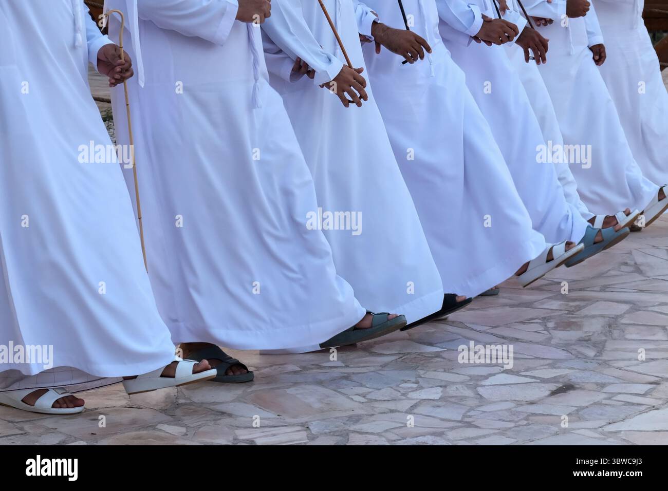 Low-angle shot of feet of Emirati men in white thobes performing folk ...