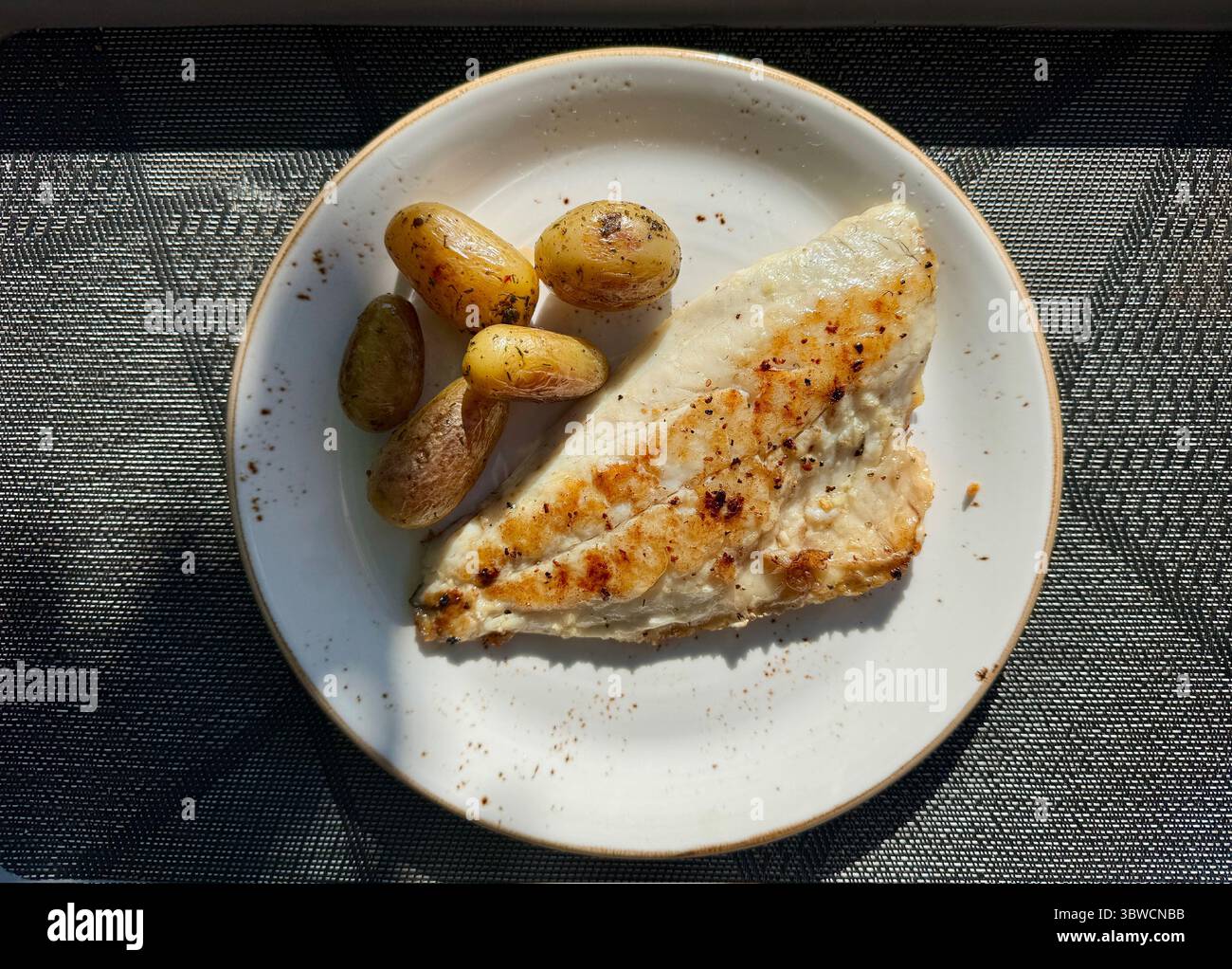 plate of freshly grilled fish fillet and potatoes on sunny table ...