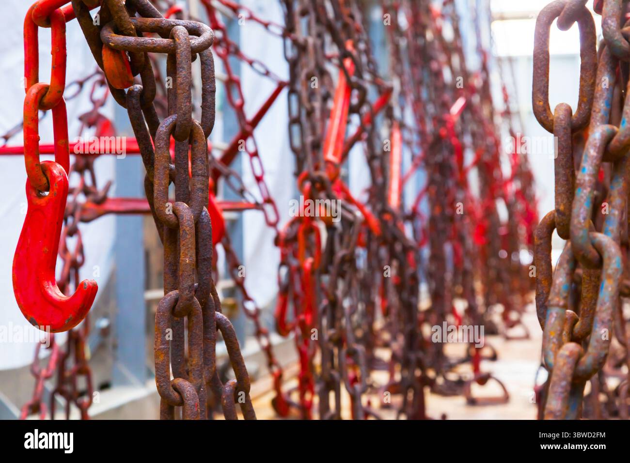 Many rusty red chains with hooks are fastened and hold containers with ...