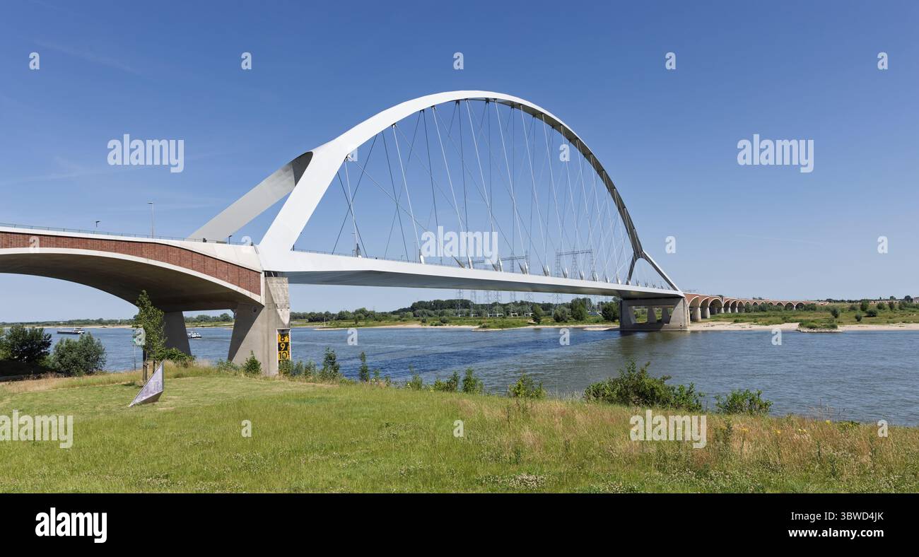 Modern white arch bridge "De Oversteek" spanning a wide river under a ...