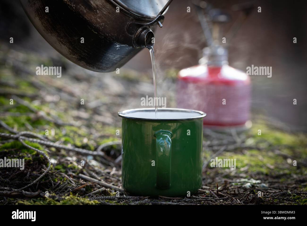 Boiling water is poured from worn metal kettle into green enamel mug on ...