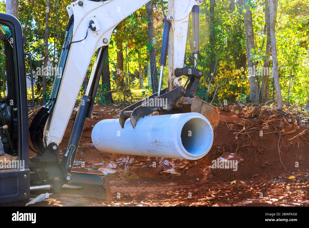 An excavator is in action, lifting large cement pipe amidst ...