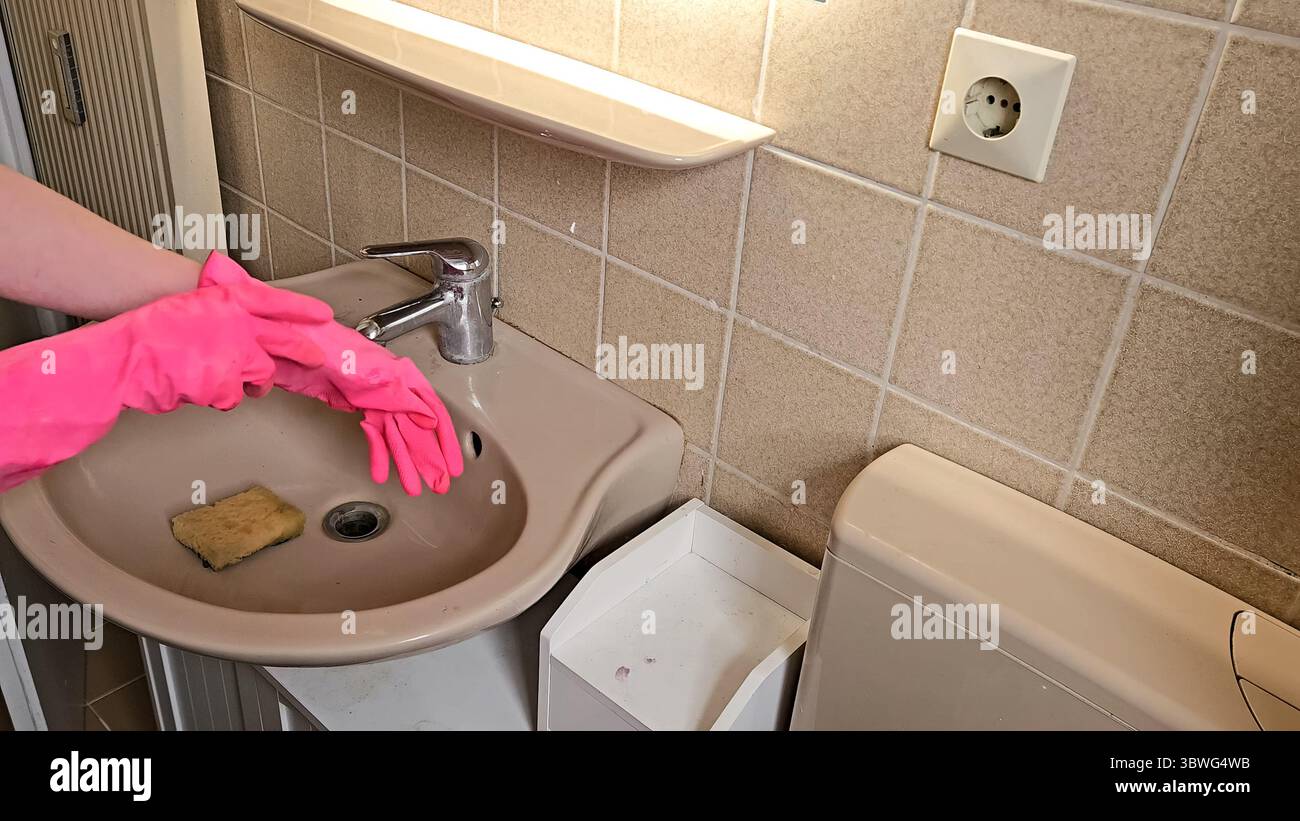 Woman preparing to clean a bathroom by putting on pink rubber gloves at ...