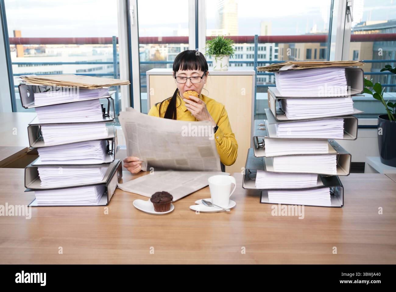 Secretary eats muffin and reads newspaper, piles of files next to her ...