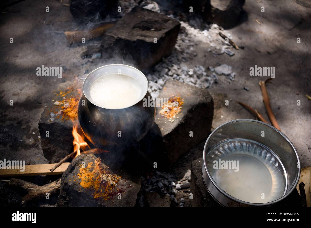 A black pot simmers over an open flame while spices surround it ...